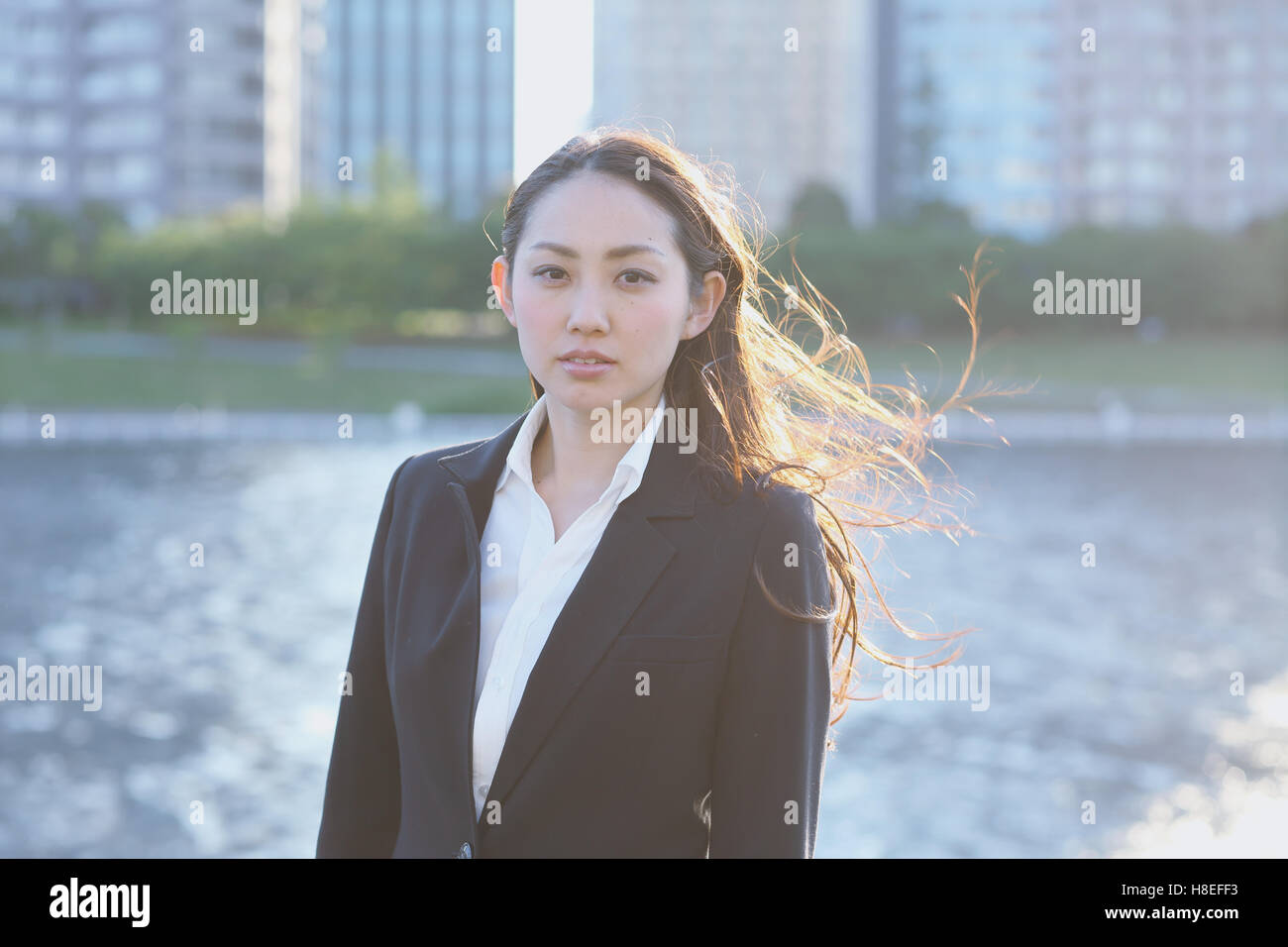 Portrait of young Japanese businesswoman by a river downtown Tokyo ...