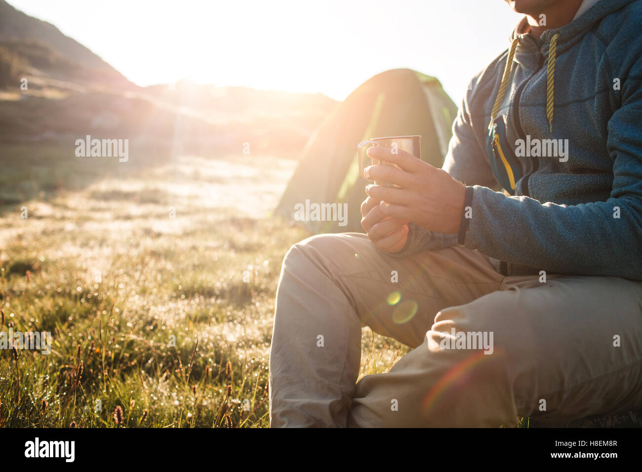 Young man drinking tea at sunrise in mountains. Mountain camping ...