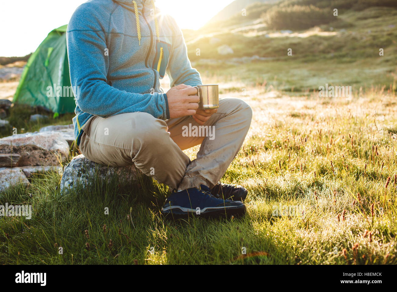 Young man drinking tea at sunrise in mountains. Mountain camping ...