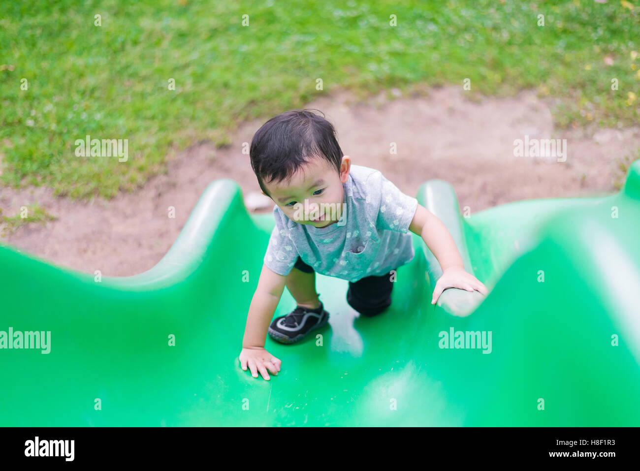 Little Asian kid climbing up the slide at the playground under the ...