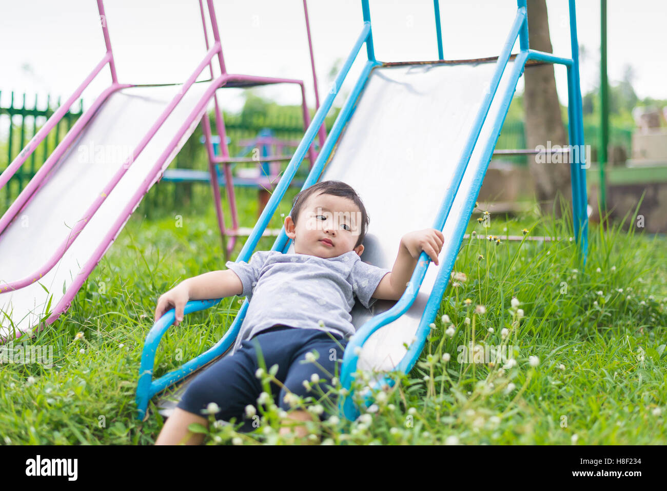 Little Asian kid playing slide at the playground under the sunlight in ...