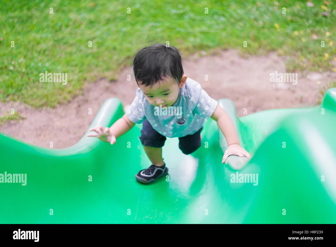 Little Asian kid climbing up the slide at the playground under the ...