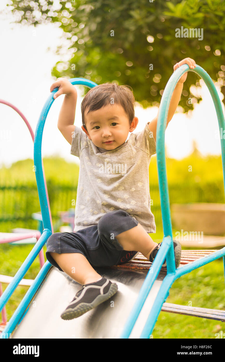 Little Asian kid playing slide at the playground under the sunlight in ...