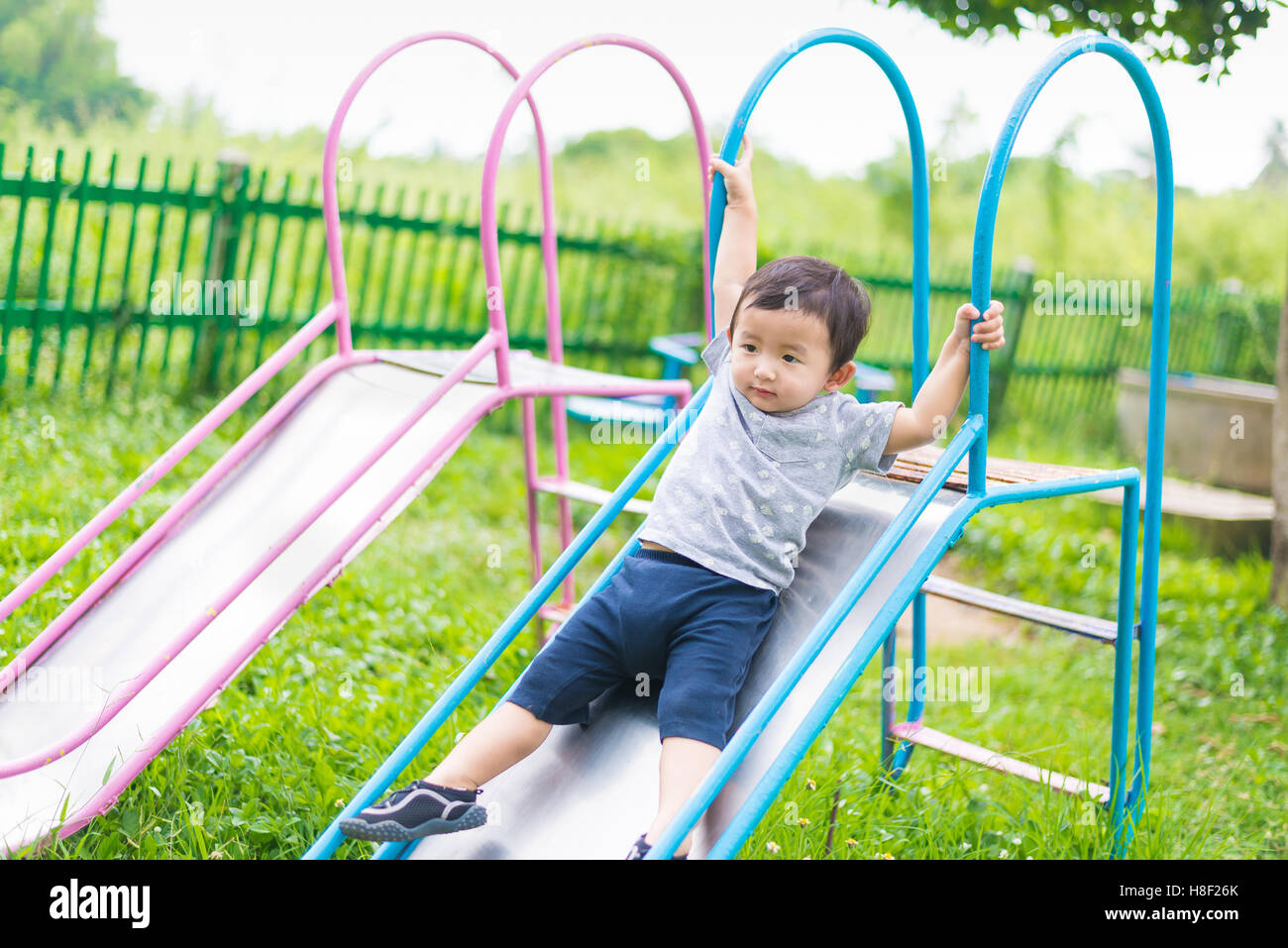 Little Asian kid playing slide at the playground under the sunlight in ...