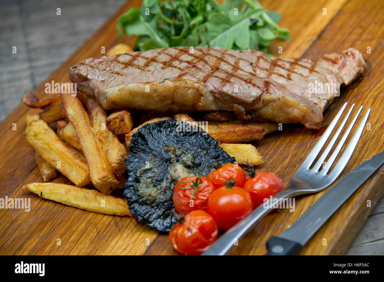 Steak & chips with mushrooms and tomatoes served on a wooden platter. a ...