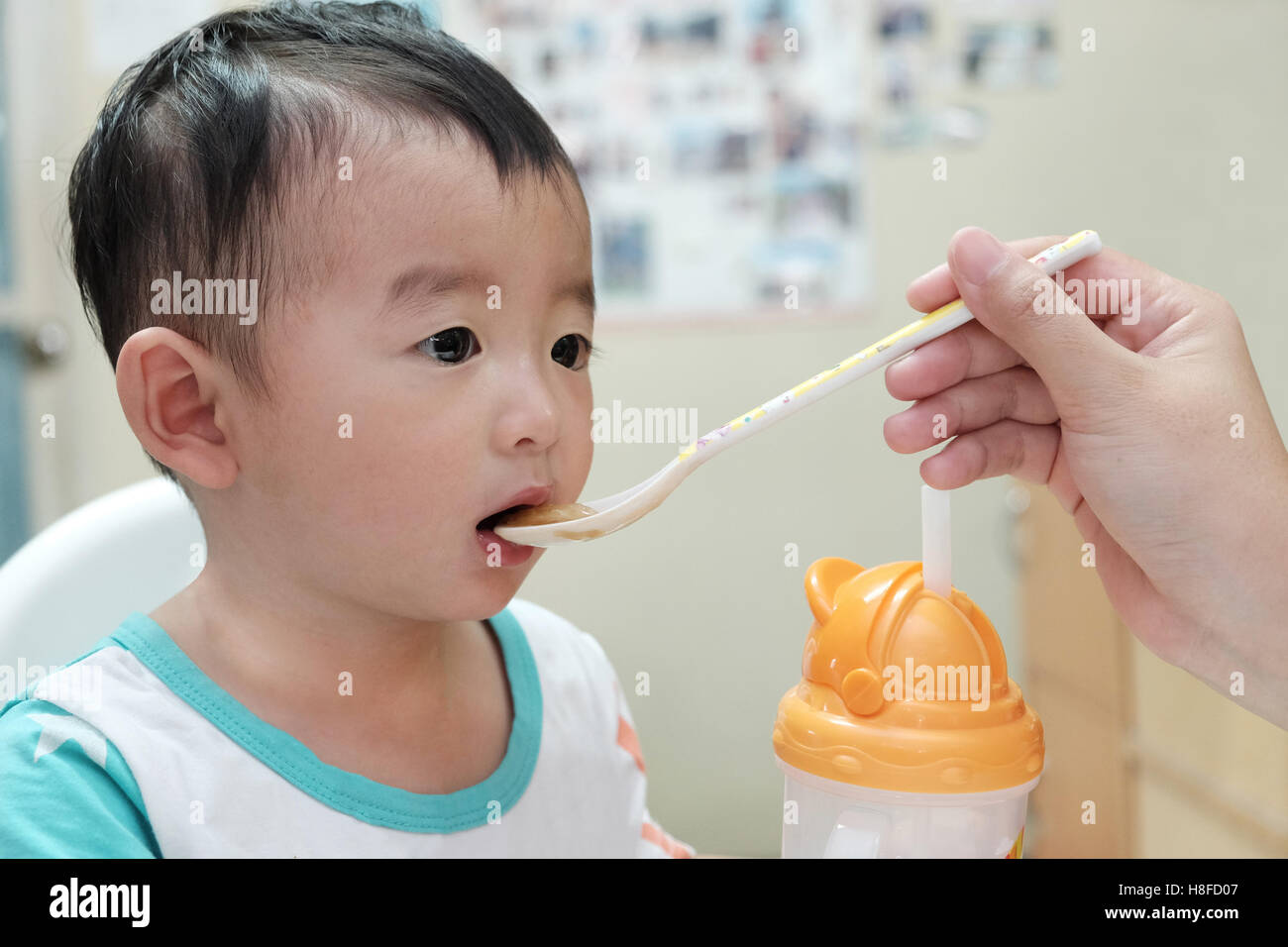 Closeup of Asian kid boy eating with spoon on highchair, mother is ...