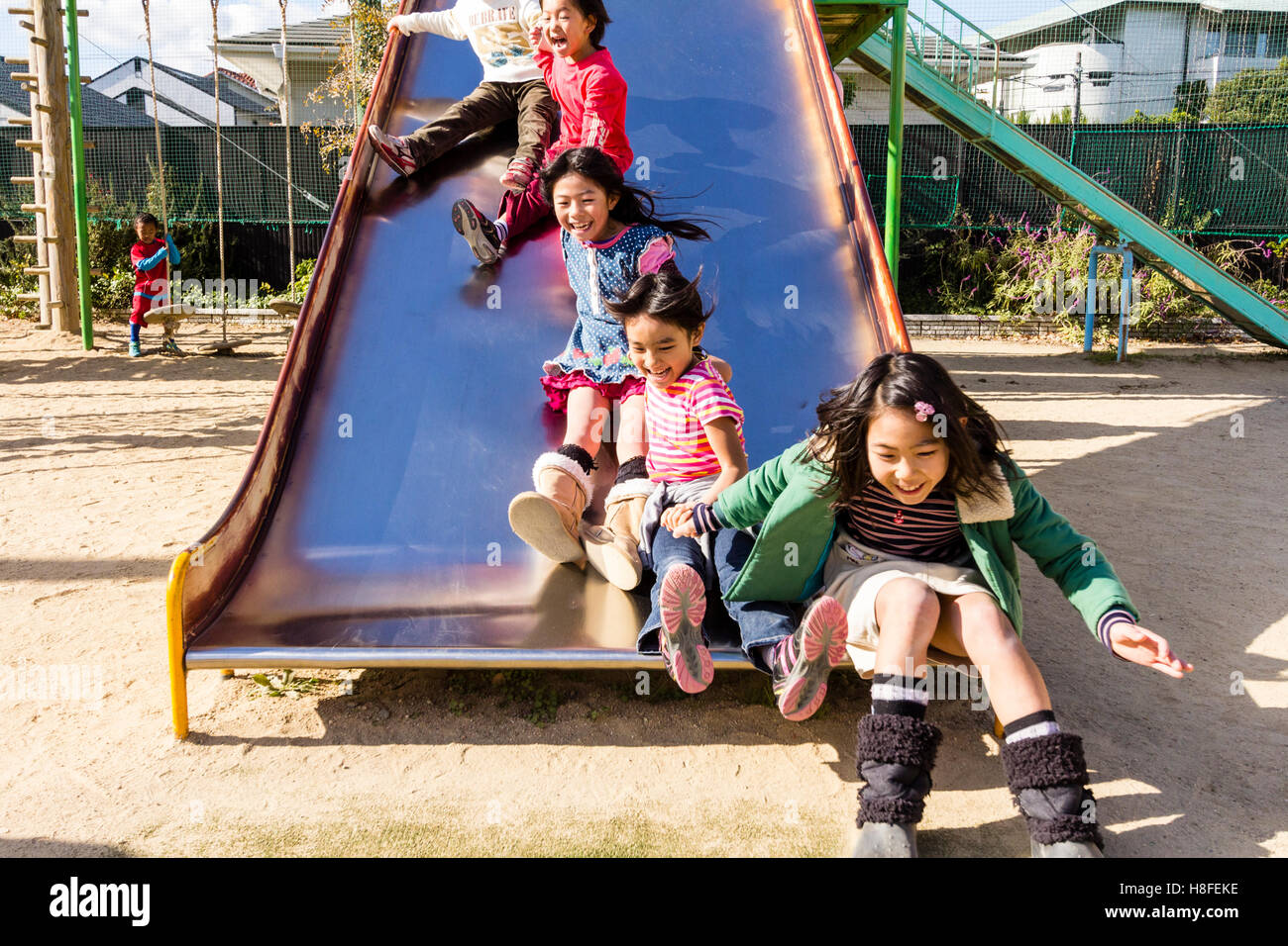 Japan. School playground. Children, three girls, 6-8 years old, jumping ...