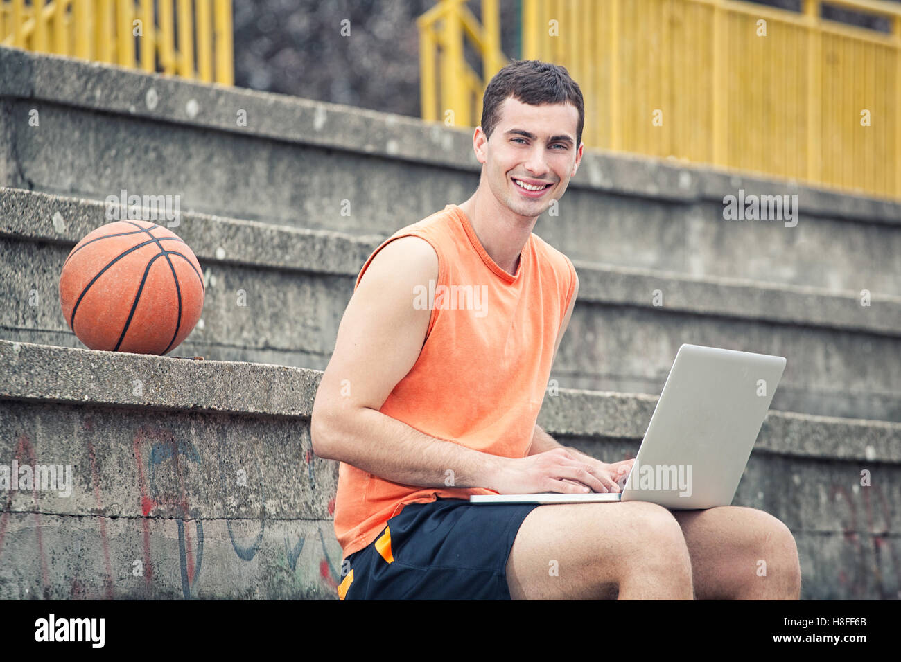 Smiling Caucasian basketball player using a laptop outdoors Stock Photo ...