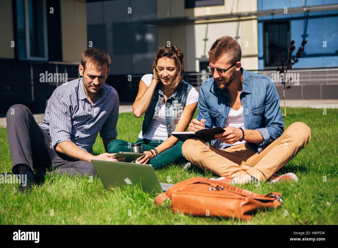 three students sitting on lawn Stock Photo - Alamy