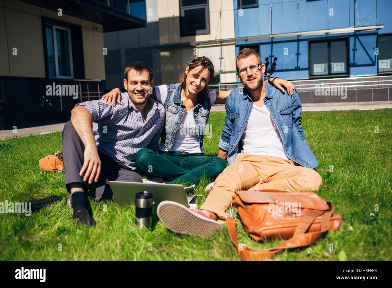 three happy students sitting on lawn Stock Photo - Alamy