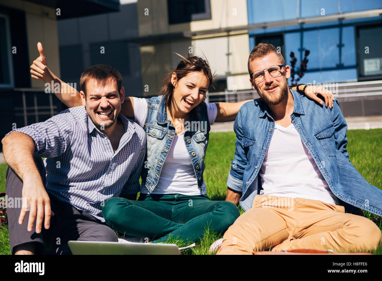 three happy students sitting on lawn Stock Photo - Alamy