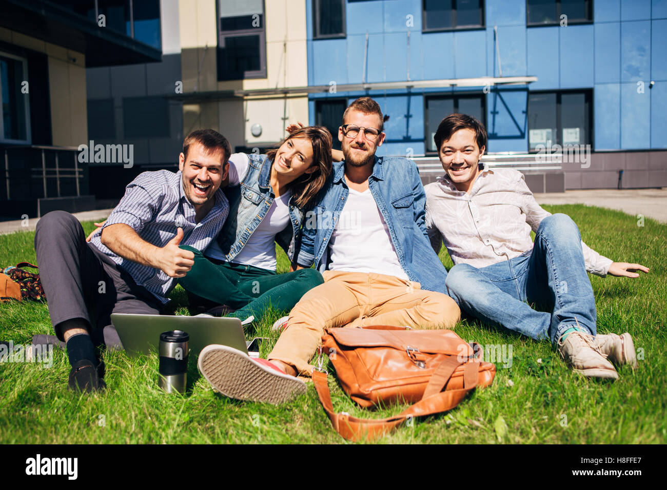 Four happy students sitting on lawn Stock Photo - Alamy