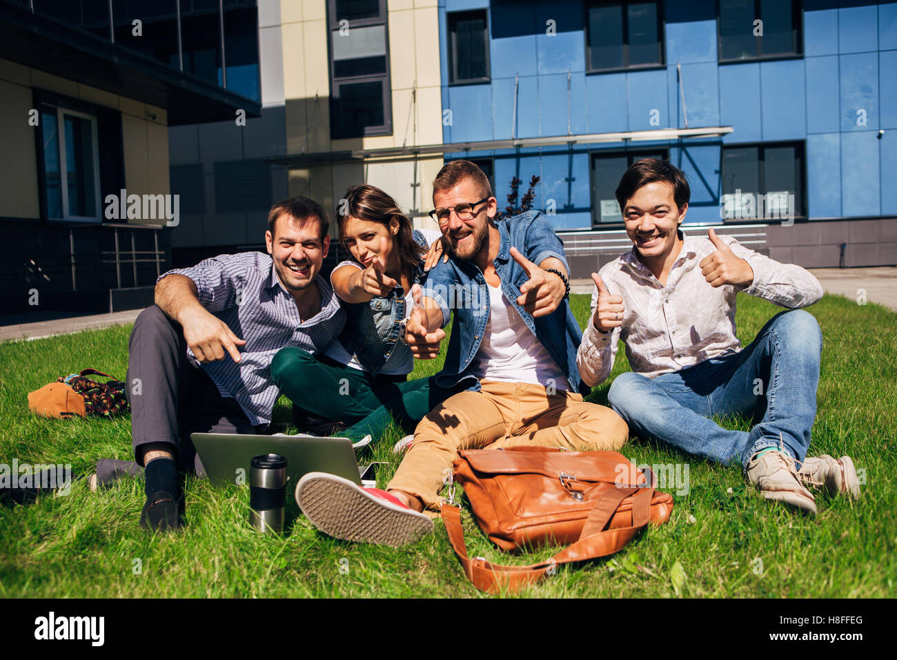 Four happy students sitting on lawn Stock Photo - Alamy