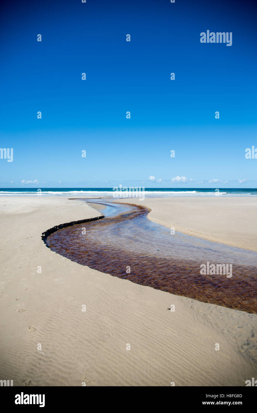 Curved creek water stream along sand toward waves on beach Stock Photo ...