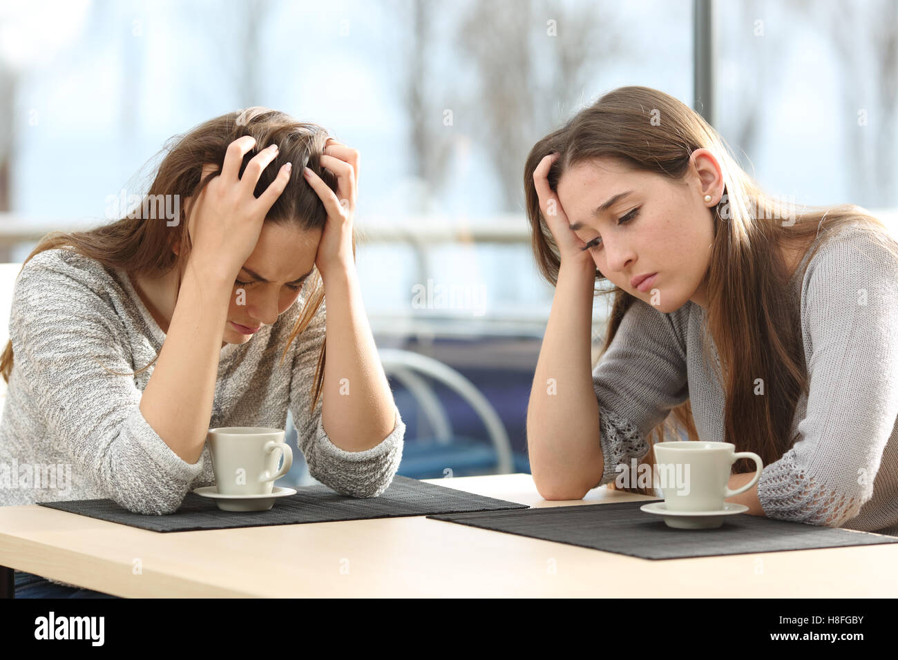 Two sad women worried in a coffee shop with a window in the background ...