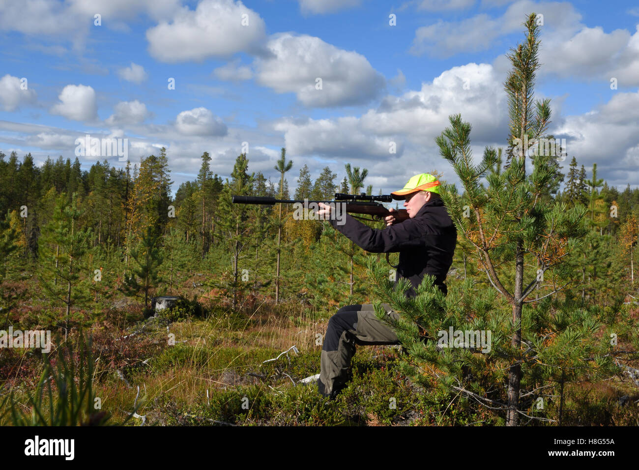 Young female moose hunter sitting on a stump aiming with her rifle with ...