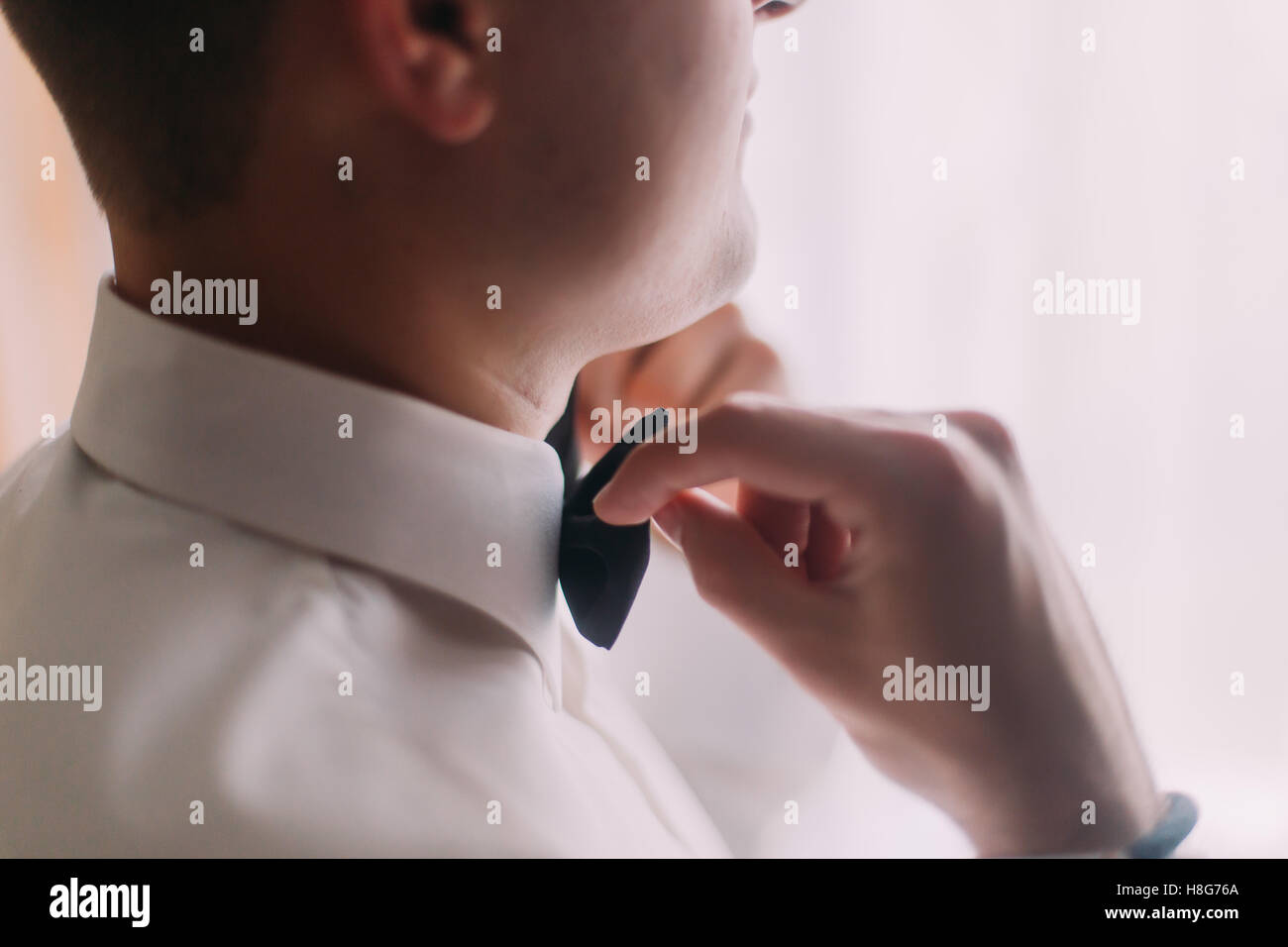 Handsome groom tying his bow-tie in the morning of wedding day. Close ...