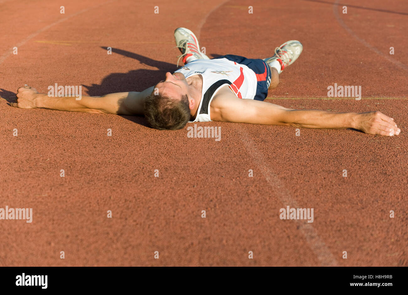 Exhausted sportsman lying on running track Stock Photo - Alamy