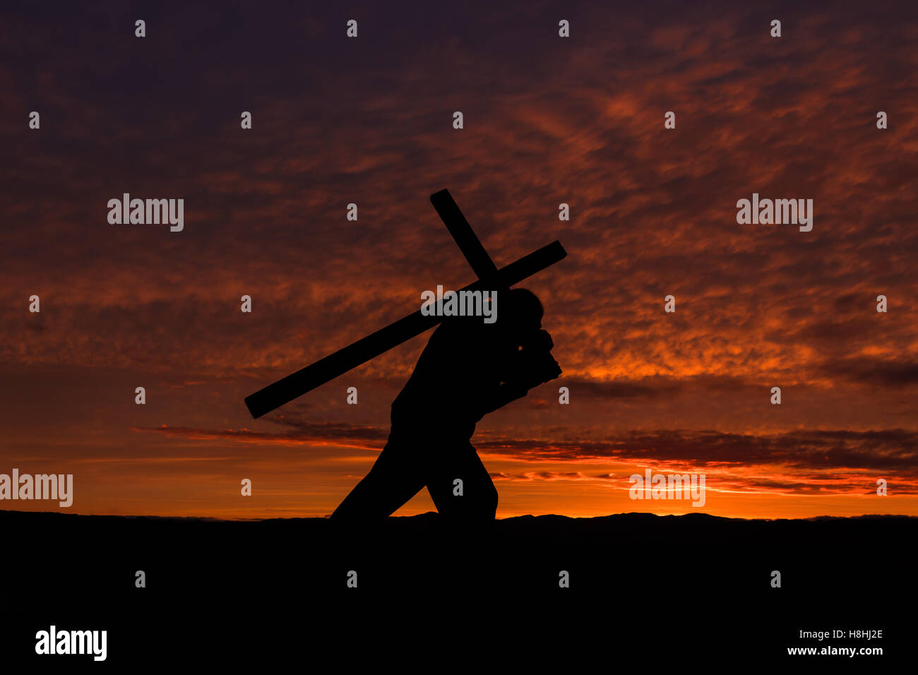 Man carrying a cross on his back with a dawn clouded sky in the ...