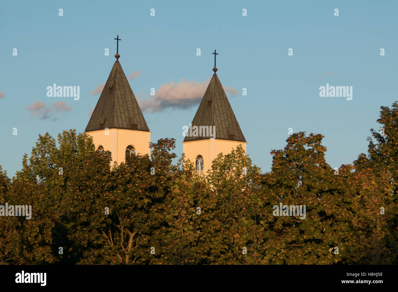 Twin steeples of a catholic church erecting behind trees in sunset ...