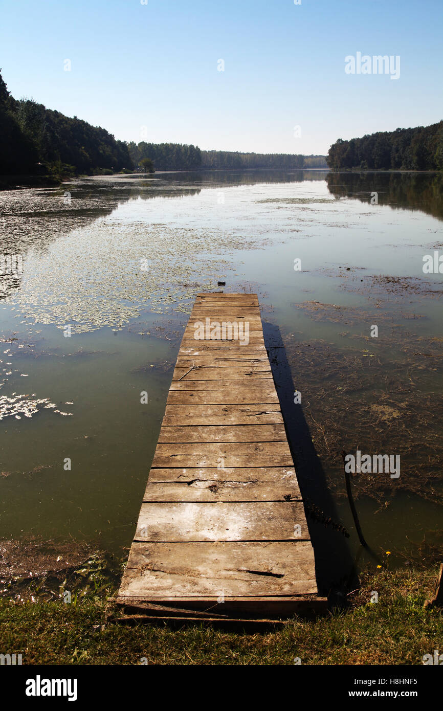 Small old lake pier made from wood on surface of water on early morning ...