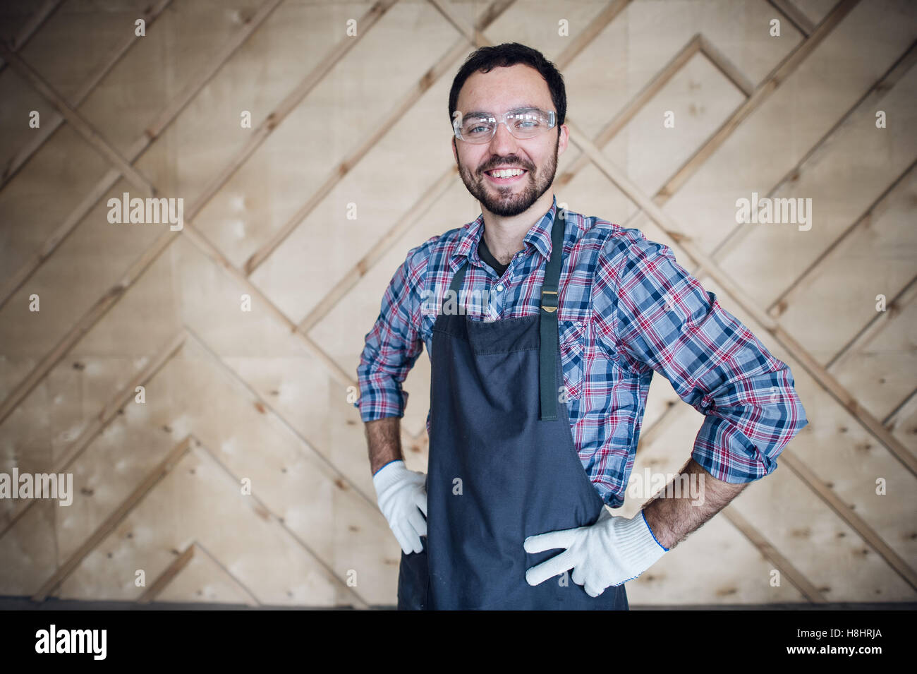 Young male carpenter wearing gloves and glasses with hands on hips ...