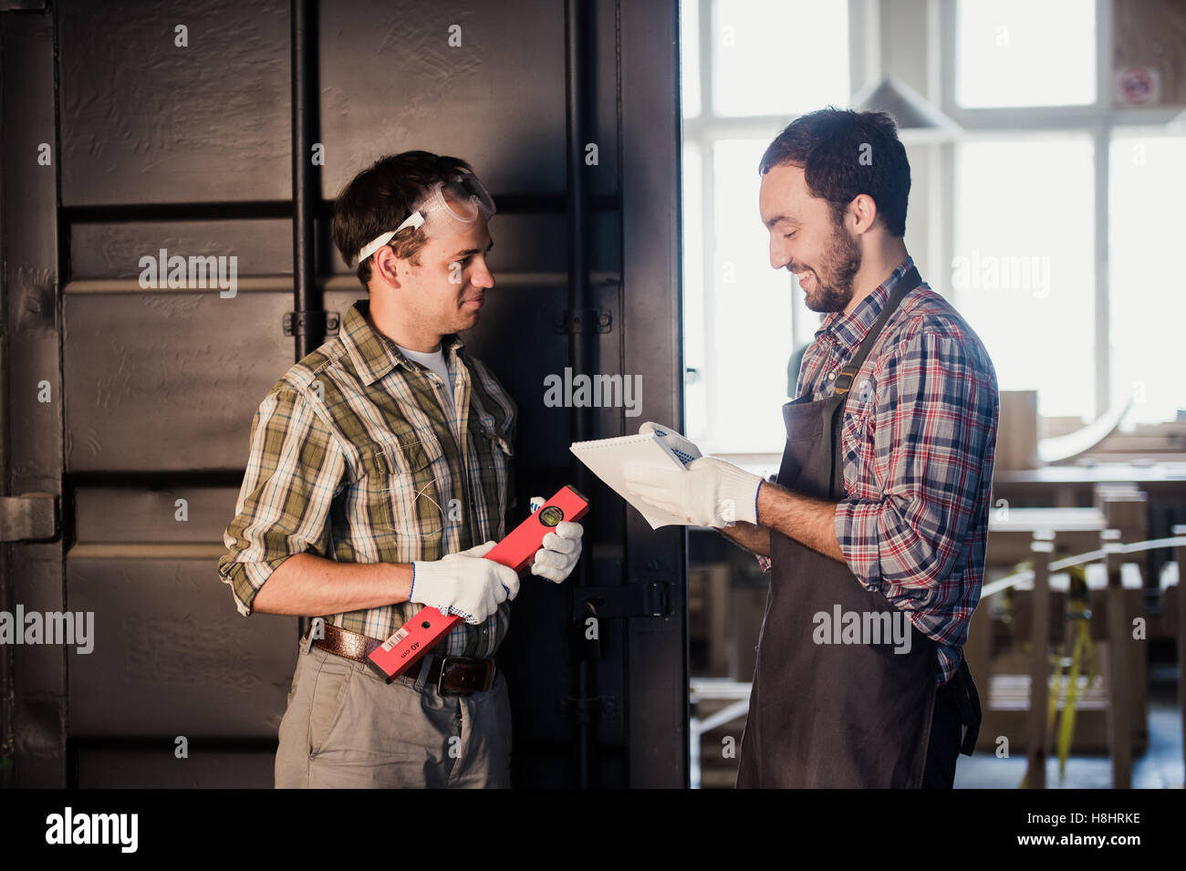 Two carpenters are talking while holding papers and ruler. One of them ...