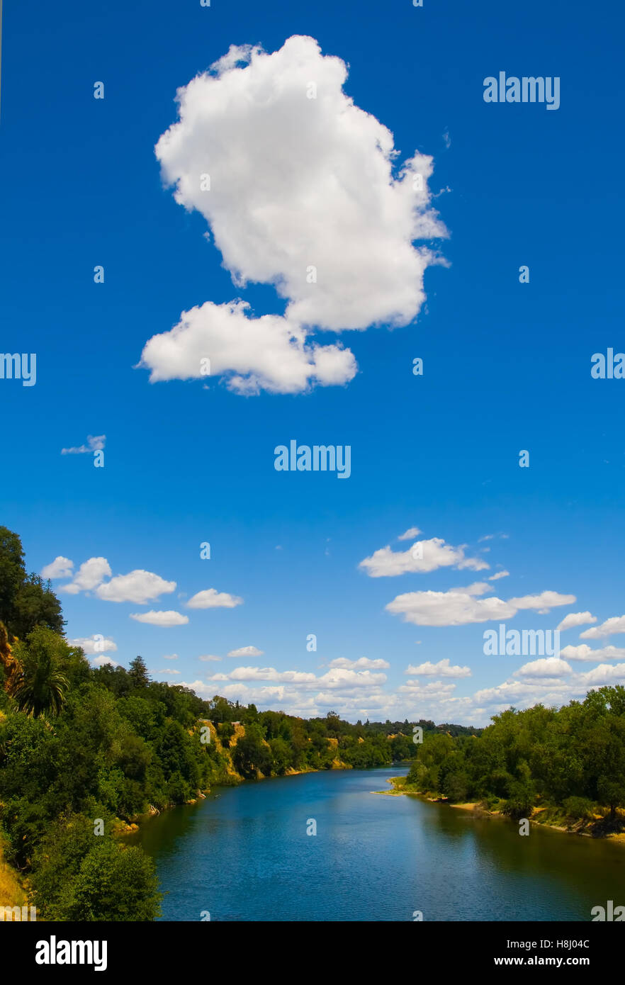 Lots of white clouds over a clean blue river with lots of trees around ...