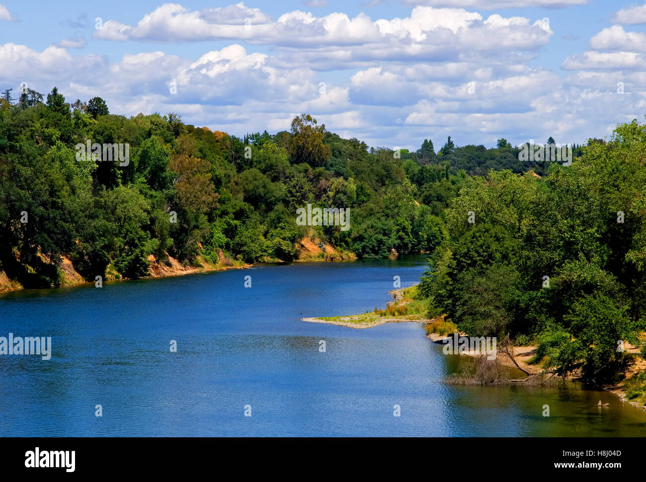 Lots of white clouds over a clean blue river with lots of trees around ...