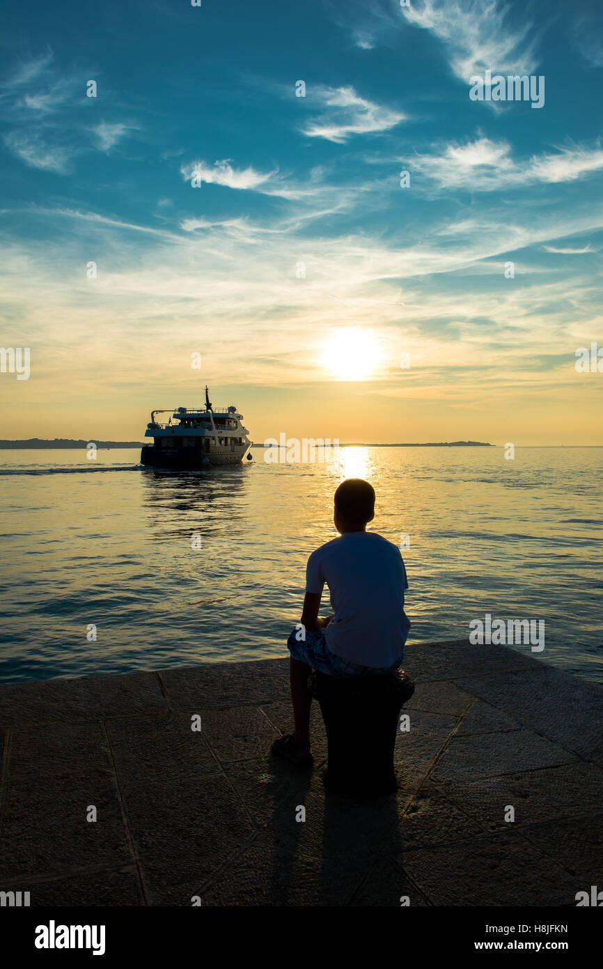 Boy on Jetty Watching Leaving Ship at Sunset Stock Photo - Alamy