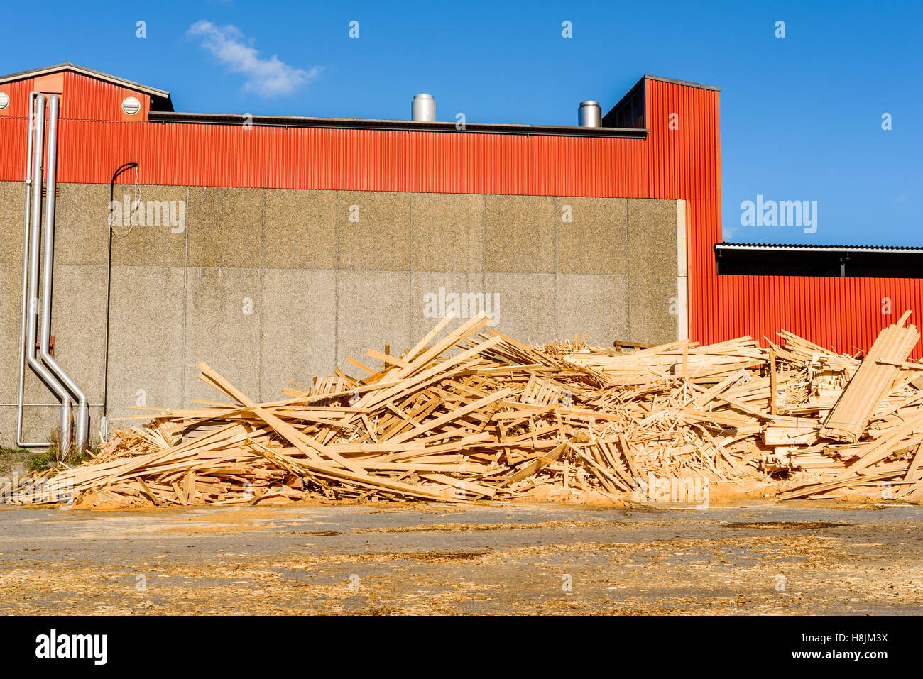 Pile of wooden debris in front of red industrial building. The wood is ...