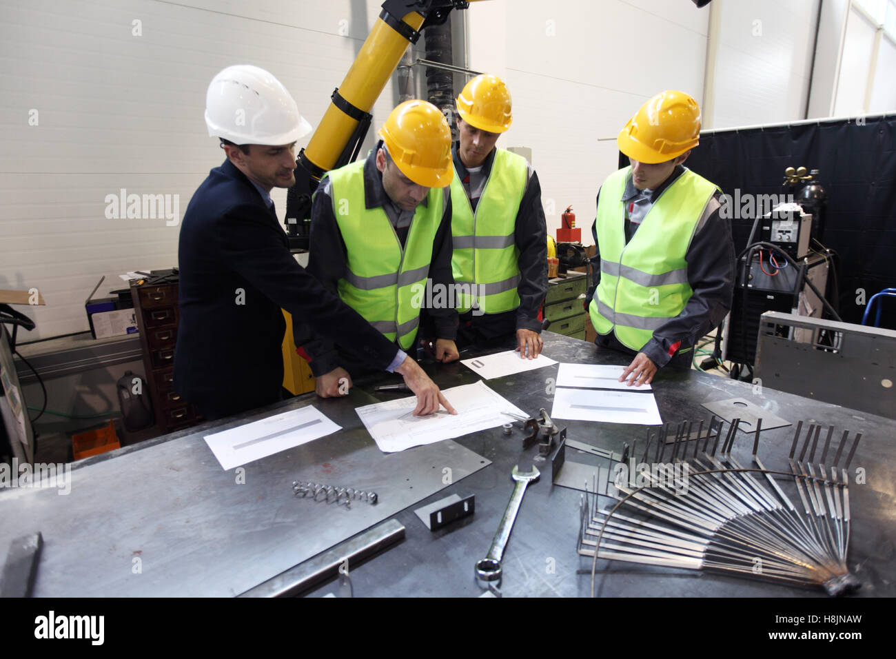 Workers and manager in safety helmets working with documents at factory ...