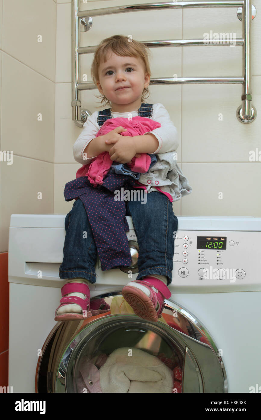 Happy cute little girl with clothes sitting on the washing machine in ...