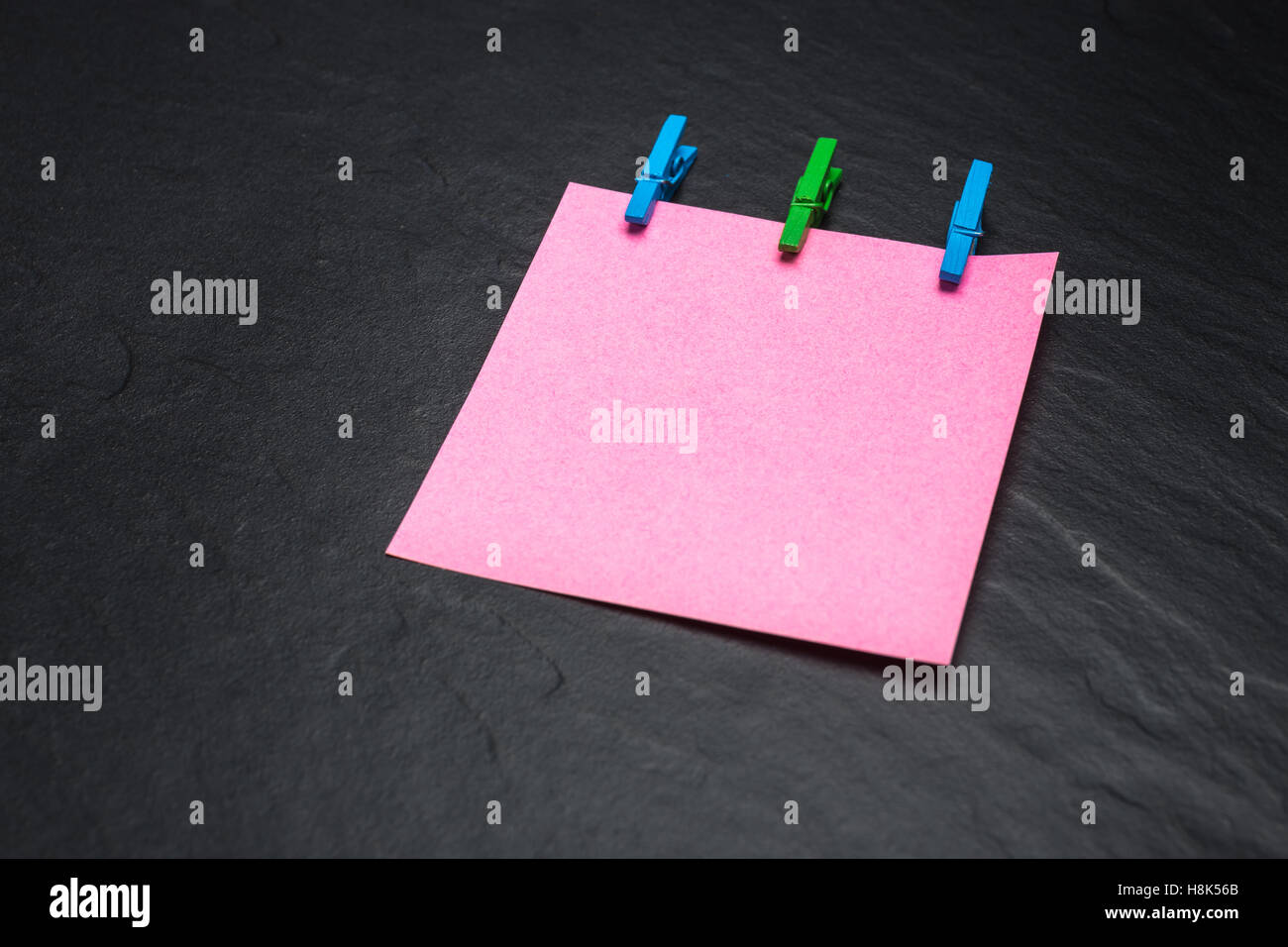 close up of a pink note paper and clothes pegs on a black background ...