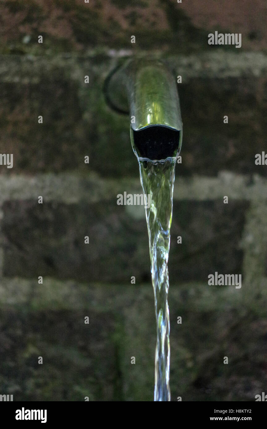 Close up of running water from a tap with brick wall in background ...