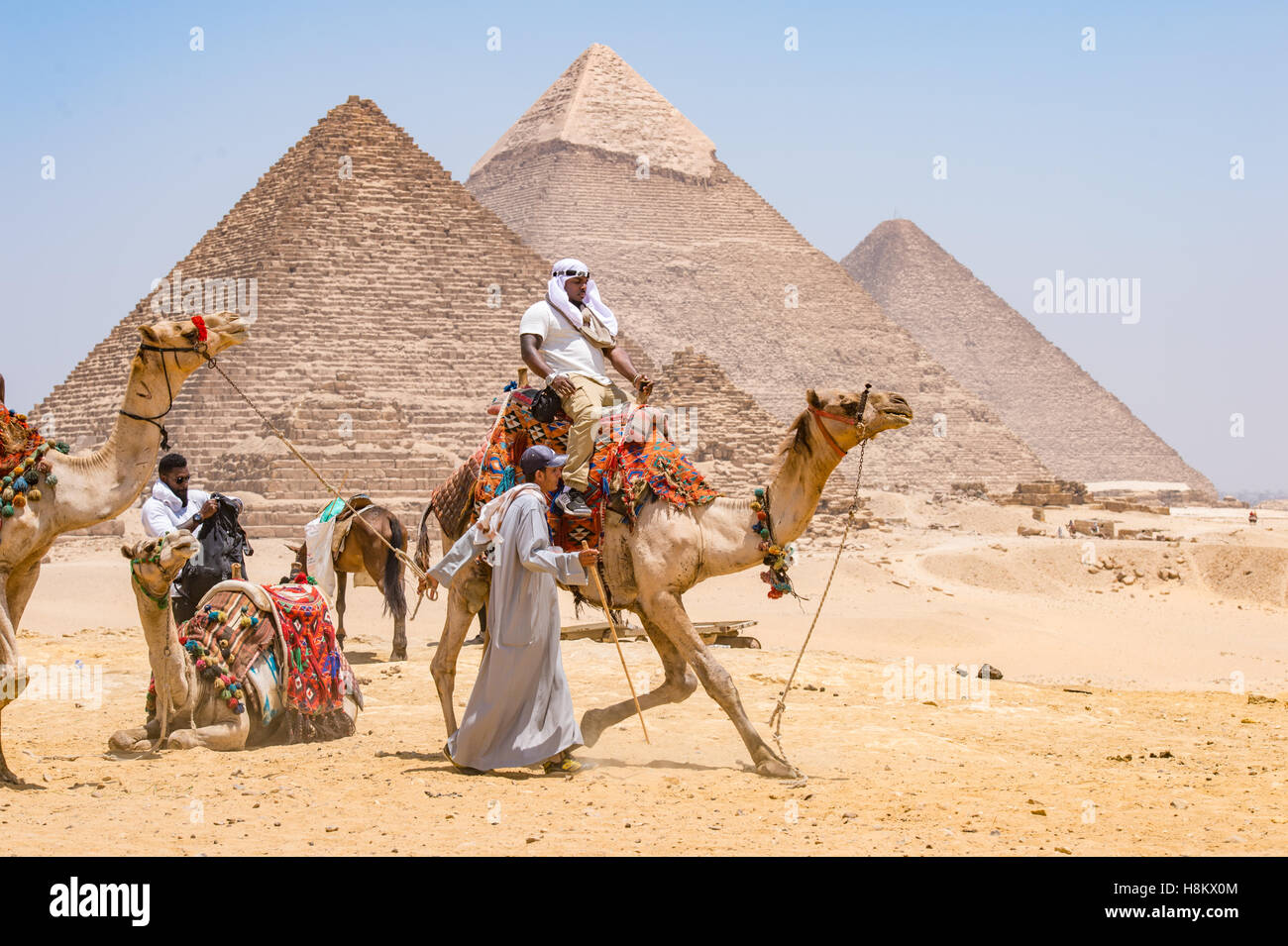 Cairo, Egypt Tourists and camel drivers with their camels walking through the desert with the ...