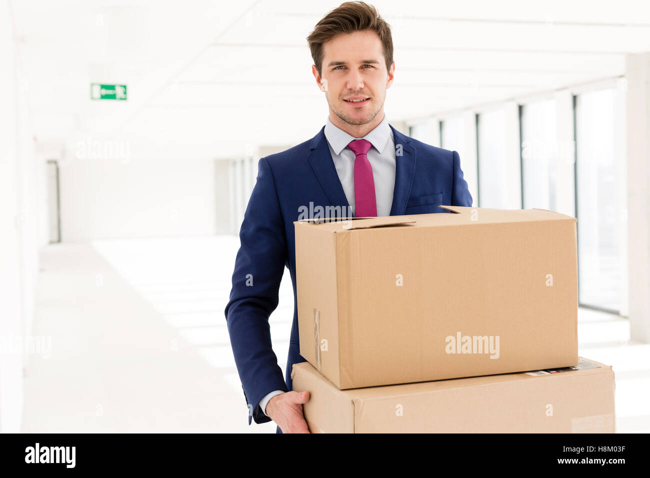 Portrait of young businessman carrying cardboard boxes in new office ...