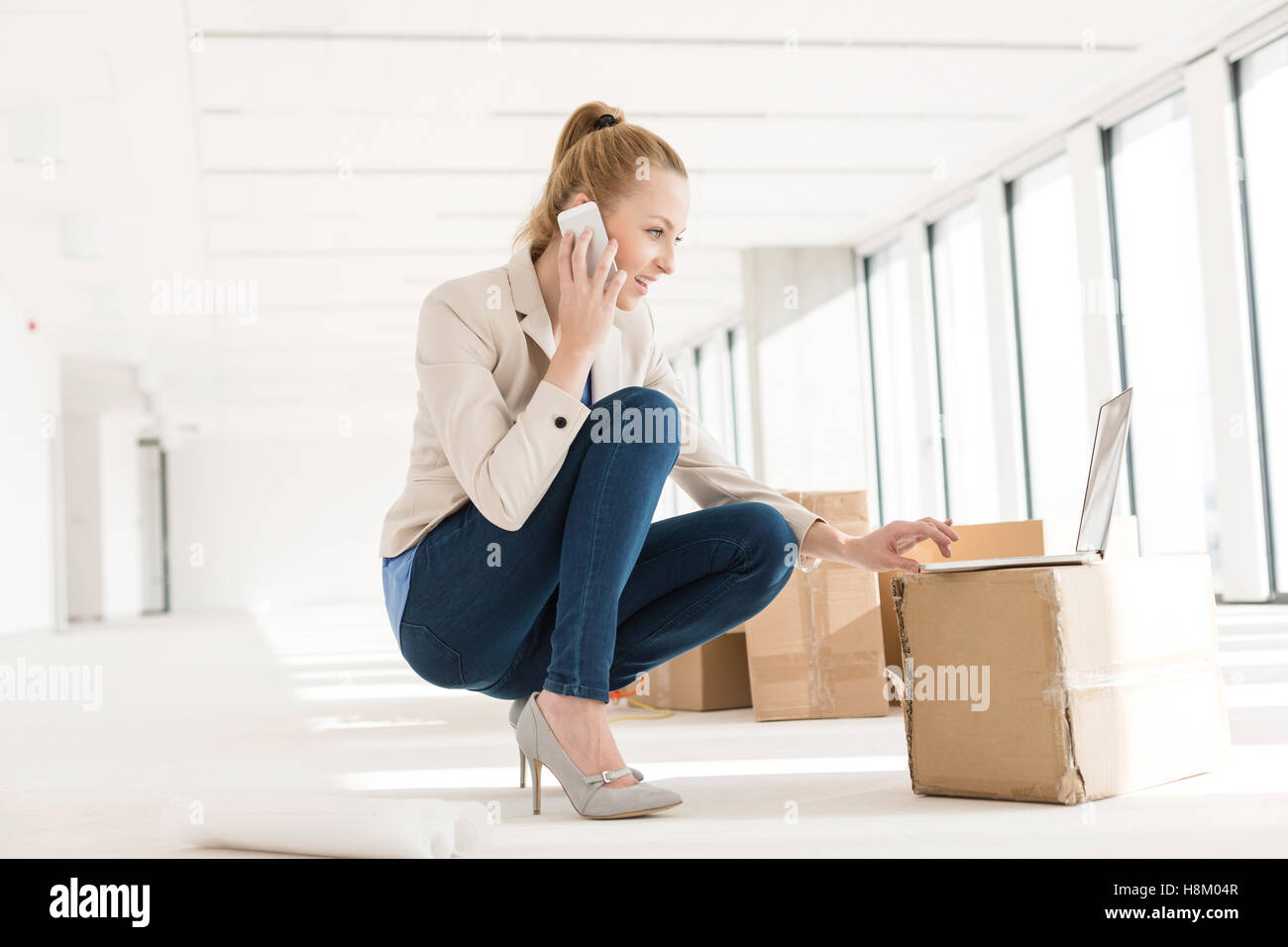 Full length of young businesswoman crouching while using mobile phone ...