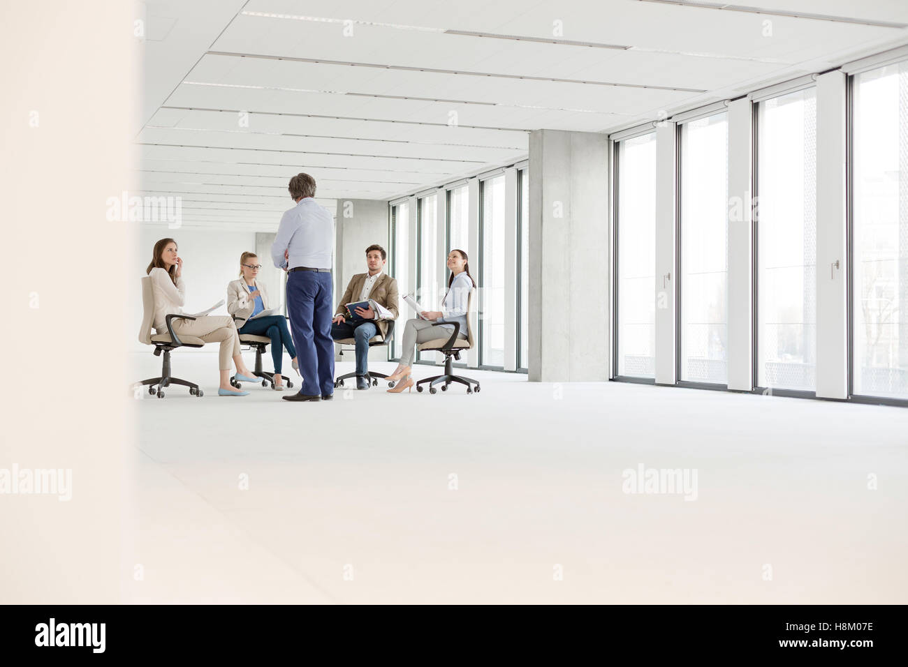 Mature businessman having discussion with colleagues sitting on chair ...