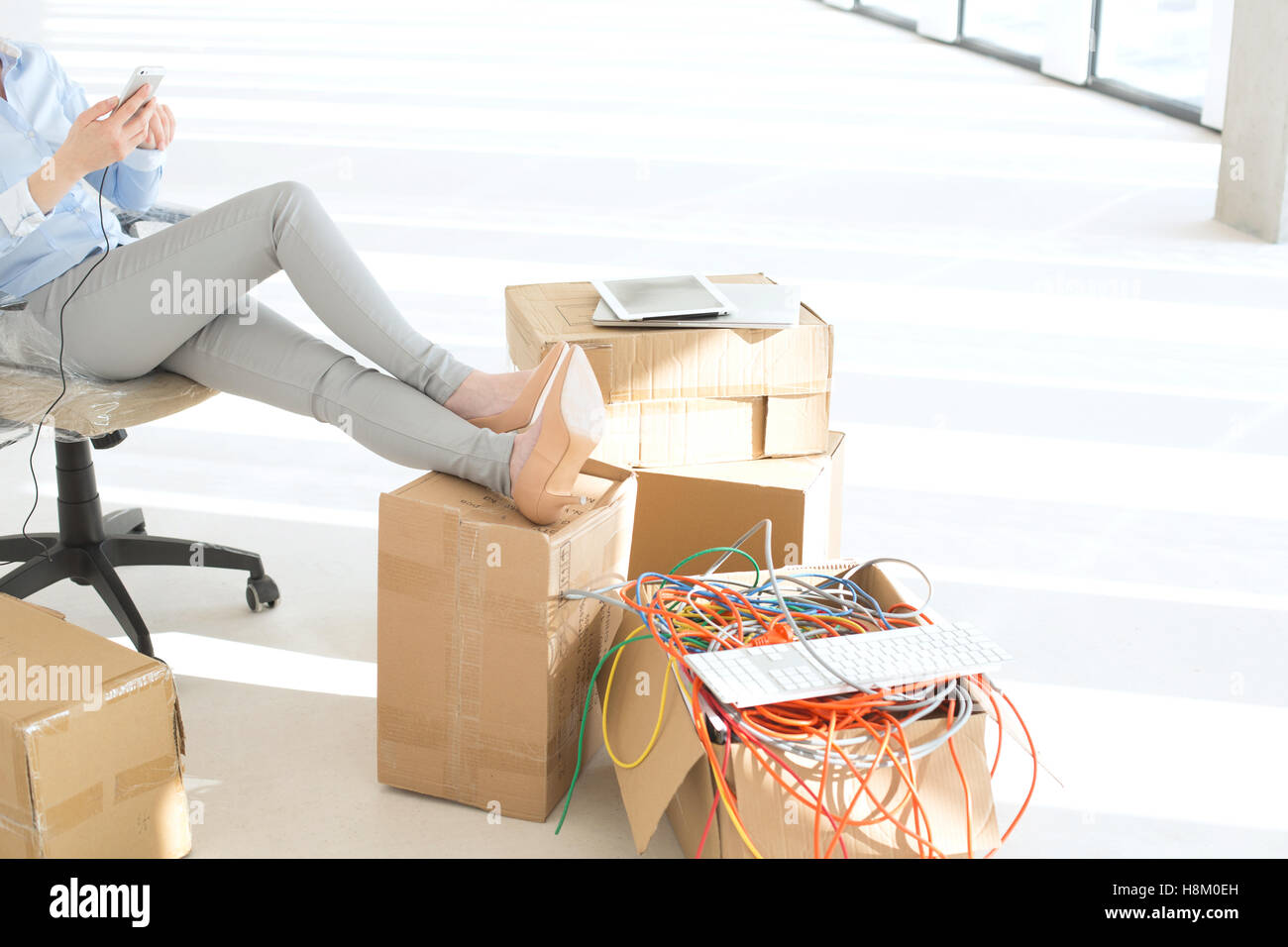 Low section of businesswoman holding mobile phone with feet up on ...