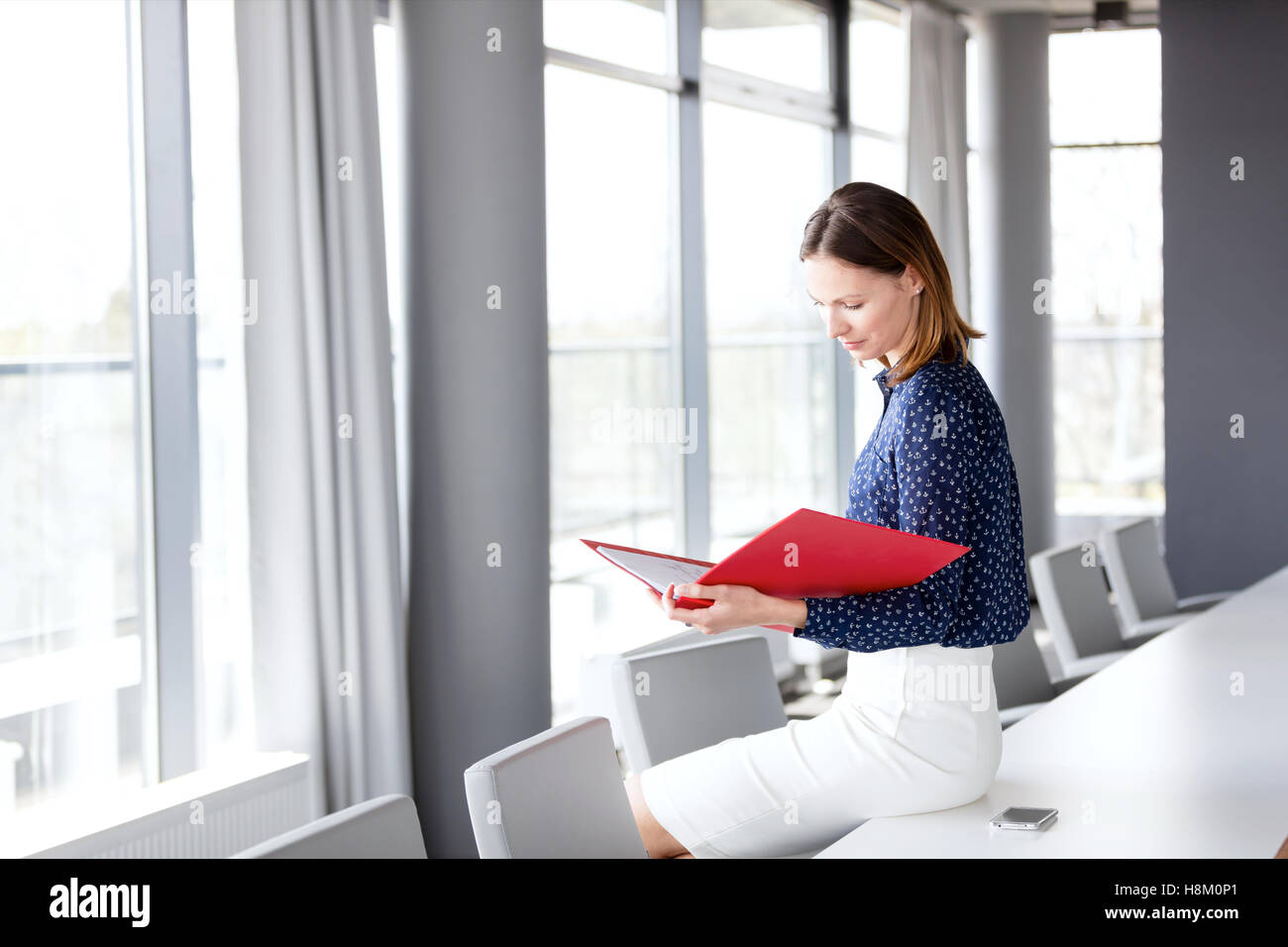Young businesswoman reading file while sitting on conference table in ...