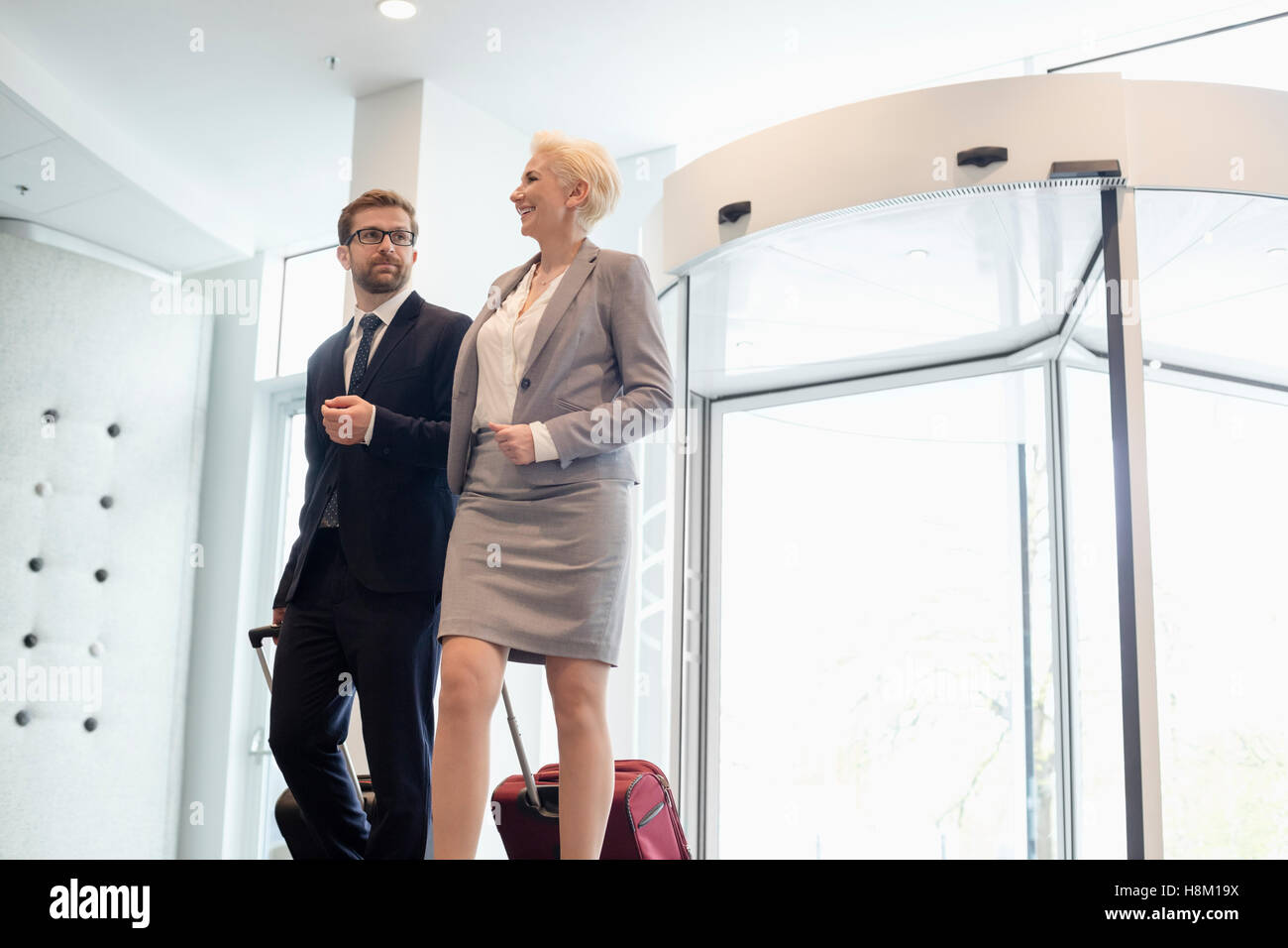 Happy business people pulling luggage while walking in convention ...