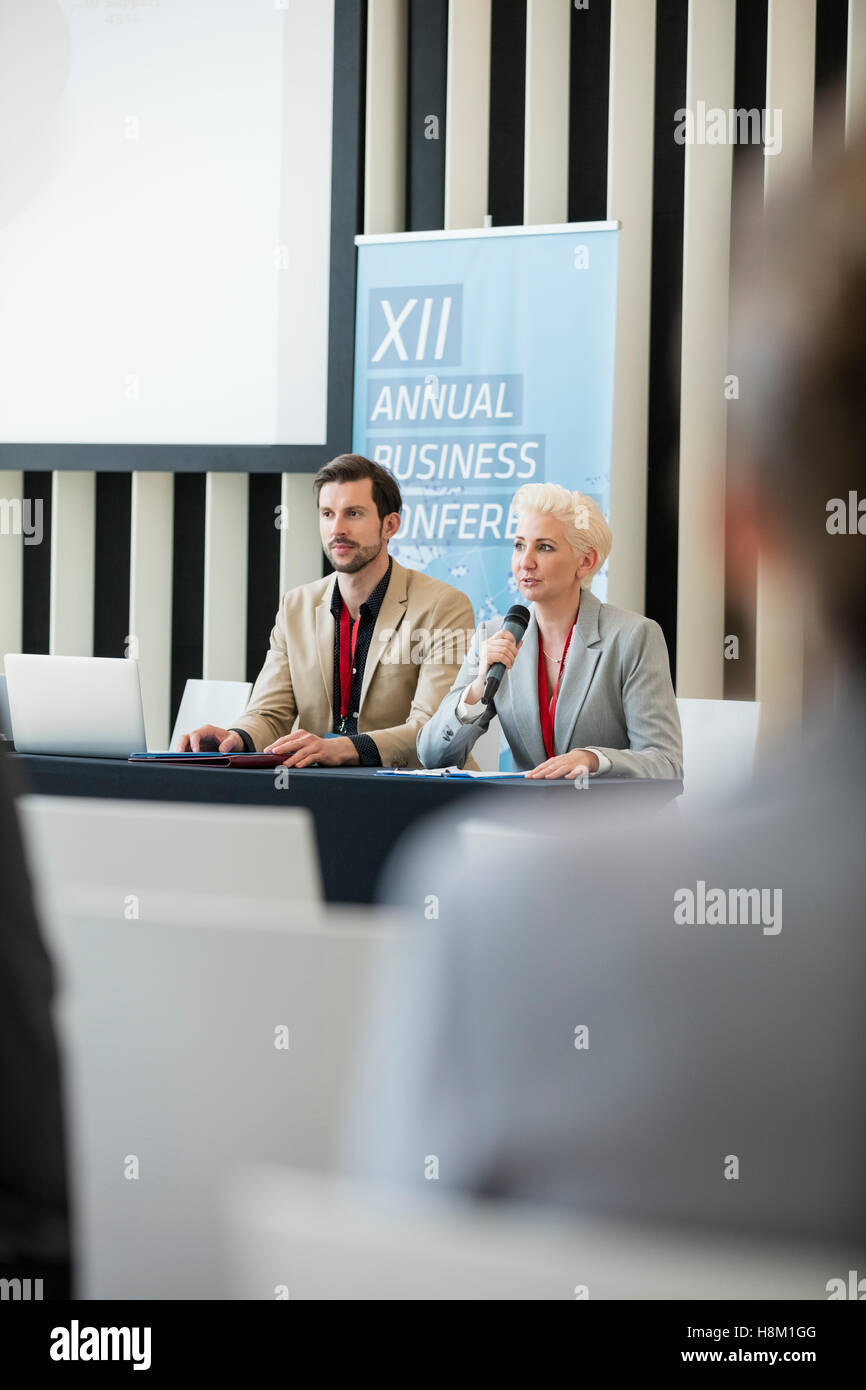 Businesswoman speaking through microphone while sitting with colleague ...
