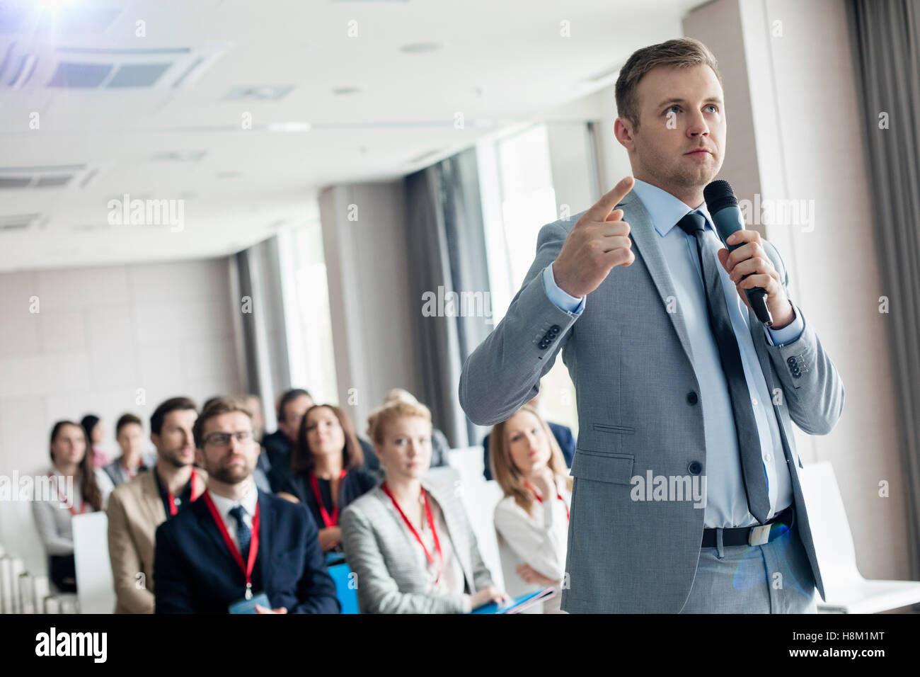 Businessman pointing while speaking through microphone during seminar ...