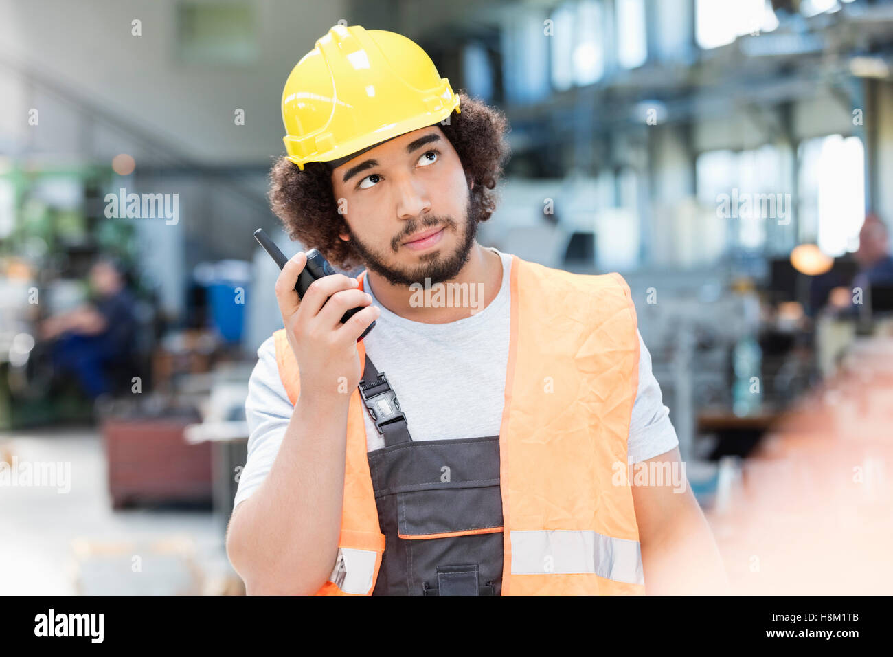Young manual worker listening to walkie-talkie while looking up in ...