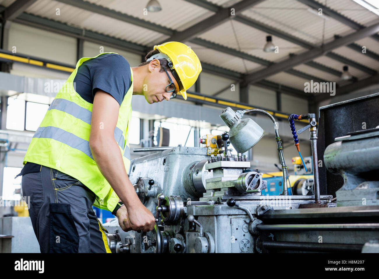 Side view of mid adult male worker operating machinery in metal ...