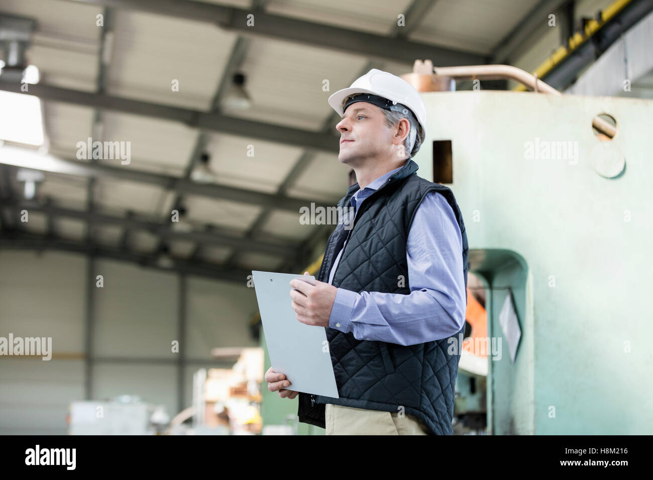 Side view of male supervisor holding clipboard in metal industry Stock ...