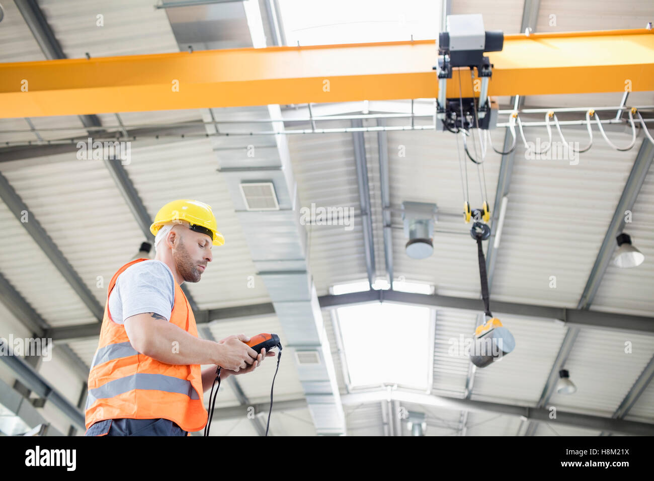 Low angle view of manual worker operating crane lifting steel in ...