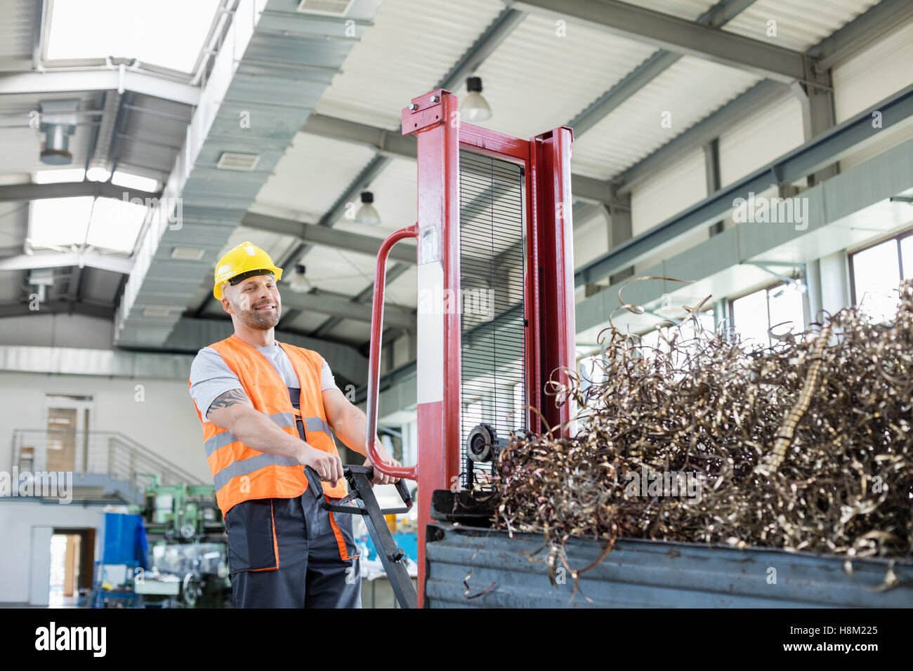 Portrait of mid adult worker pulling hand truck loaded with steel ...