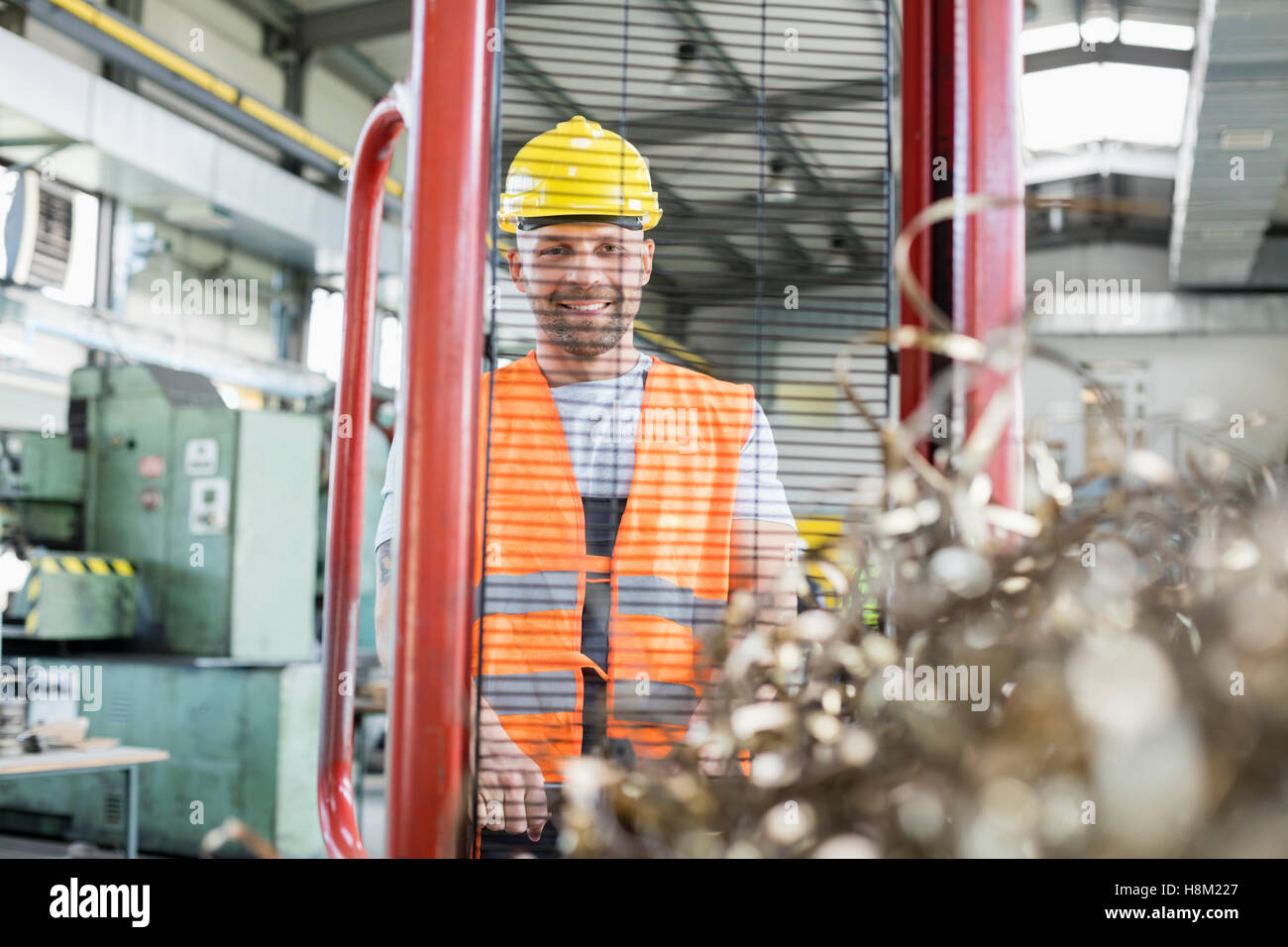 Portrait of manual worker pulling hand truck with steel shavings in ...